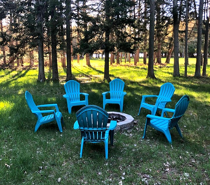 Adirondack chairs arranged in nature's conference room, where the only agenda item is relaxation. Blue chairs against green grass&mdash;Michigan's unofficial summer flag.