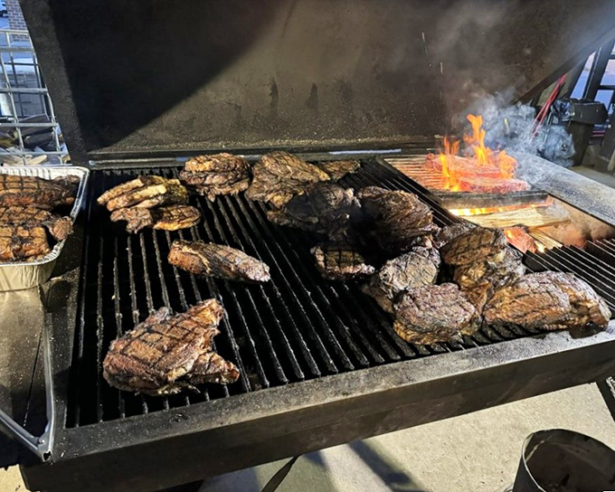 The grill master's canvas in action. Each steak sizzling toward perfection while flames dance around them like culinary pyrotechnics.