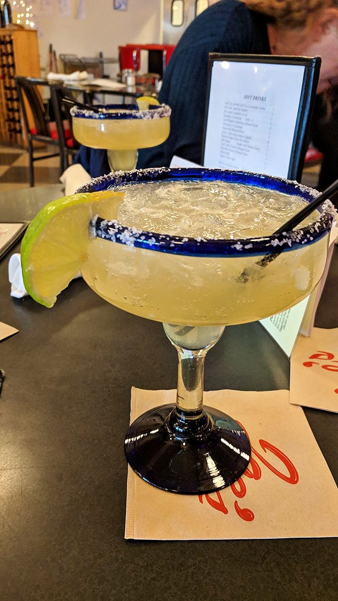 The margarita's salt-rimmed blue glass promises what it delivers: a perfectly balanced cocktail that's both vacation and therapy in one sip.