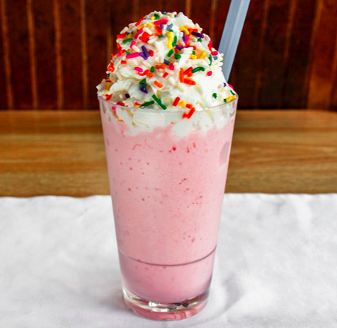 A strawberry milkshake topped with whipped cream and rainbow sprinkles&mdash;childhood nostalgia served in a glass tall enough for grown-up appetites.