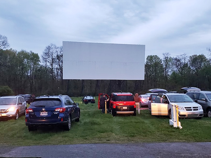 As dusk approaches, cars gather before the pristine screen, each vehicle becoming a private theater under the open sky.