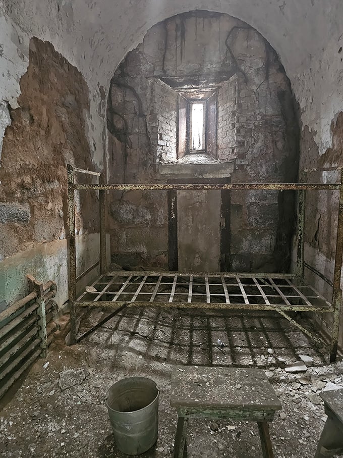 A stark reminder of confinement&mdash;rusted bed frame, crumbling walls, and a single bucket. Home sweet home for thousands over Eastern State's operational years.