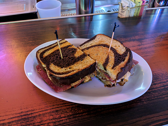 Marbled rye holding together what appears to be a perfect Reuben. The sandwich is cut diagonally—as all great sandwiches should be—and secured with those little swords.