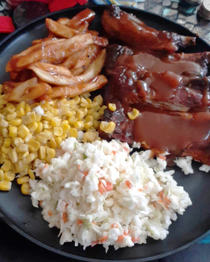 A plate that speaks the universal language of comfort—ribs, corn, slaw, and fries forming a perfect barbecue quartet.