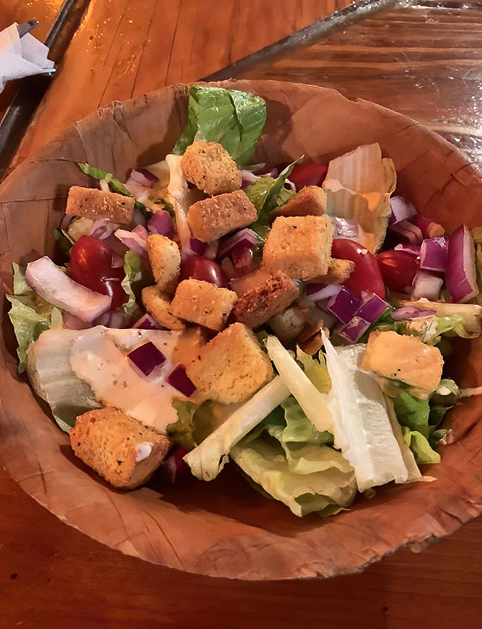 The family-style salad arrives in a wooden bowl, a fresh, crisp prelude to the meaty main event that awaits.