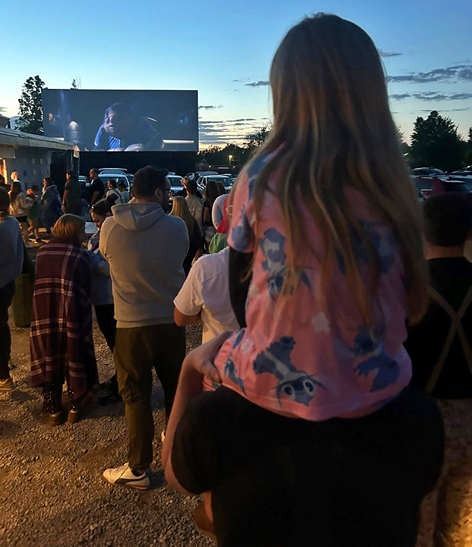 Dusk transforms the drive-in into a community gathering spot. Nothing builds childhood memories quite like watching movies perched on dad's shoulders.