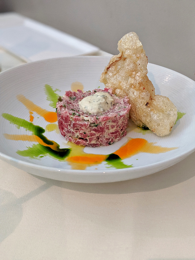 Steak tartare artfully plated with crispy accompaniments - raw perfection that would make even the most cautious diner reconsider everything.