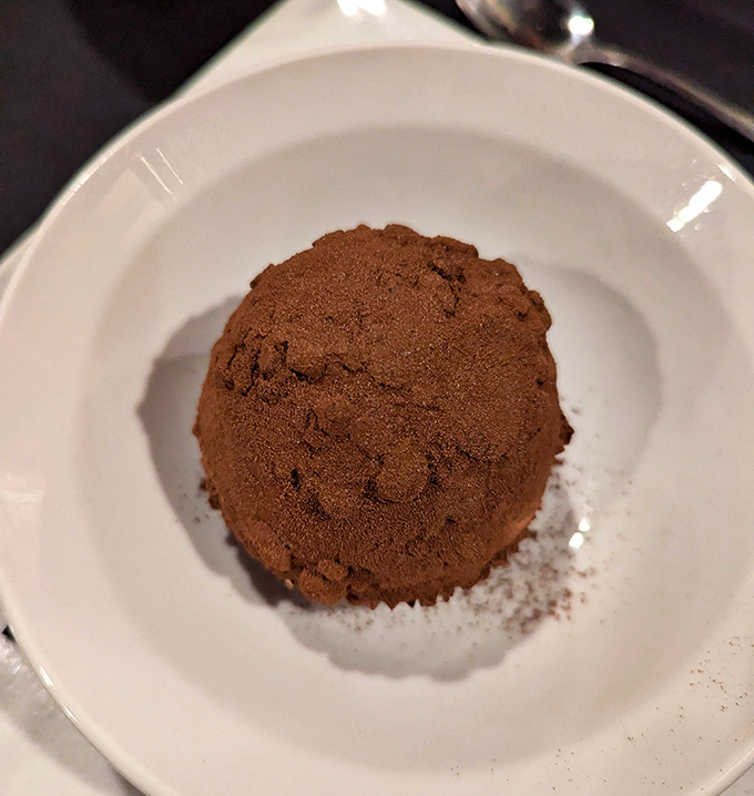 The chocolate tartufo sits like a mysterious orb of decadence, waiting to reveal its cocoa secrets with each spoonful.
