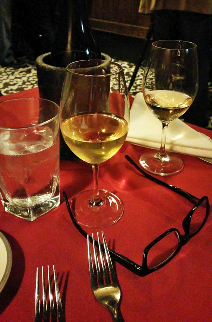 Wine glasses catching the light against that classic red tablecloth&mdash;a scene that whispers, "Tonight, we're not just eating, we're dining."