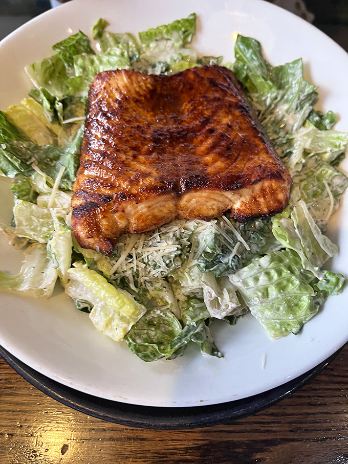 Grilled salmon perched atop a Caesar salad like it's surveying its leafy kingdom. A nod to those who want seafood without the deep-fryer guilt.