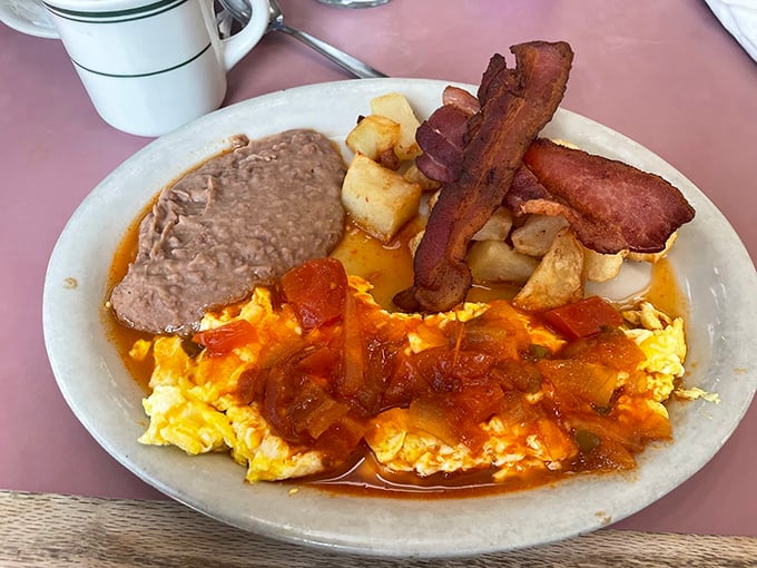A breakfast plate that understands the importance of balance: eggs bathed in ranchero sauce, beans that actually taste like something, and bacon for good measure.