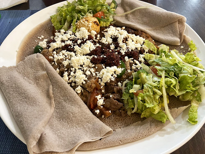 This isn't just a salad—it's a celebration of textures where crisp lettuce, savory meat, and tangy cheese find harmony atop the spongy injera base.