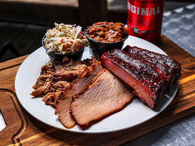 The carnivore's dream team &ndash; brisket, pulled pork, and ribs sharing a plate with coleslaw and baked beans. This wooden board holds the barbecue trifecta.