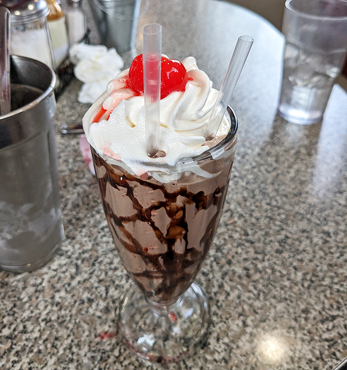 This chocolate milkshake isn't just a dessert &ndash; it's a tower of nostalgia topped with whipped cream, chocolate drizzle, and a cherry that's basically wearing a crown.