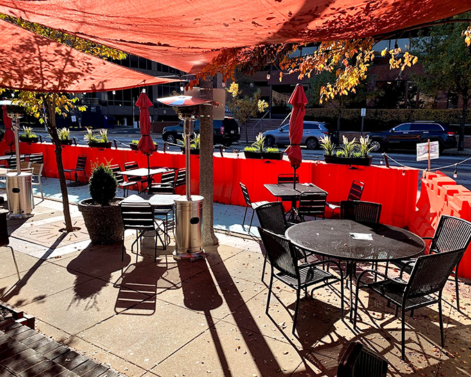 The outdoor patio, with its vibrant red barriers and shady umbrellas, transforms sidewalk dining into an urban oasis.