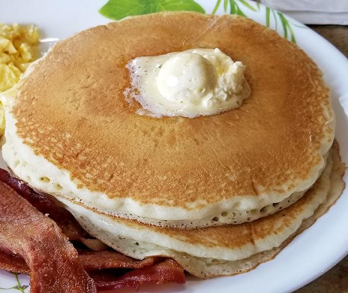 Pancakes stacked higher than your morning ambitions, with butter melting like sunshine across their golden surfaces.