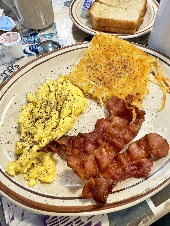Breakfast trinity: fluffy scrambled eggs, hash browns with the perfect crisp-to-soft ratio, and bacon that makes you question why we bother eating anything else.
