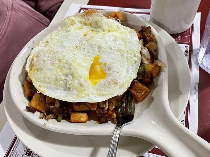 That moment when breakfast meets its destiny: a sunny-side-up egg crowning a mountain of savory hash, ready to unleash its golden treasure.