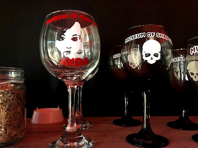 Souvenir glasses featuring Ayda's haunting visage&mdash;because nothing says "I survived" like sipping wine from a vessel adorned with the paranormal.