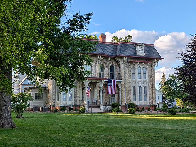 The Amos Gould House proudly wears its American flag like a badge of honor, Victorian elegance standing tall amid Michigan greenery.