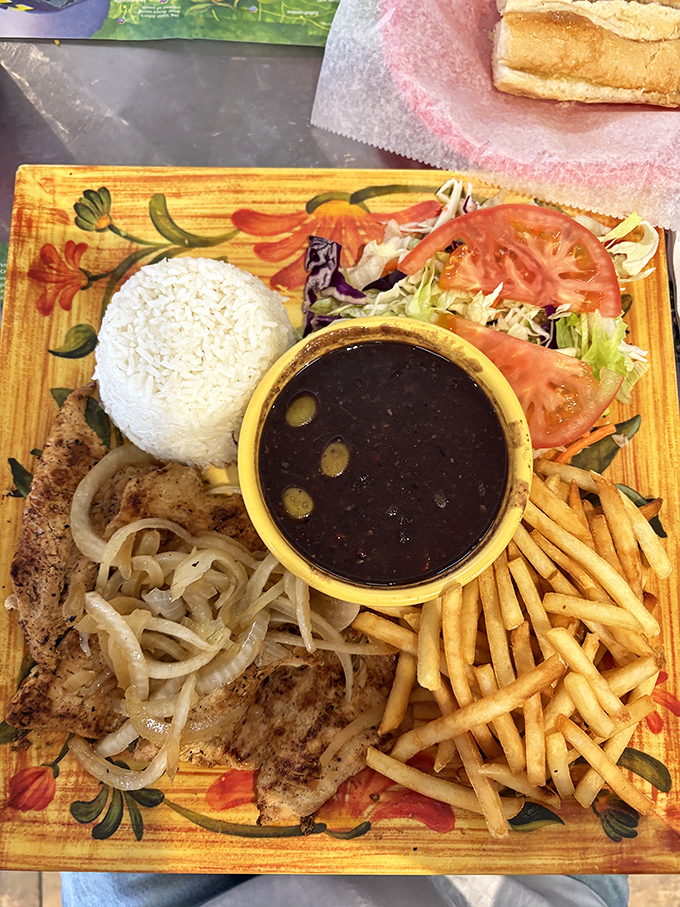 A plate that speaks fluent Cuban: tender steak, caramelized onions, and crispy fries arranged like edible artwork on a canvas of colorful ceramic.