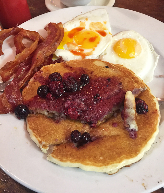 Blueberry pancakes sharing plate space with perfectly cooked eggs and bacon &ndash; breakfast's greatest hits album on a single white plate.