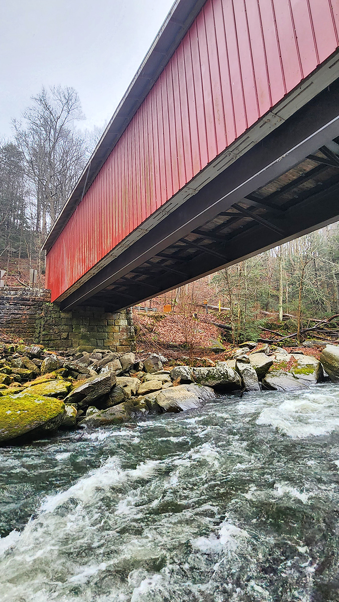From below, the bridge reveals its engineering secrets &ndash; massive stone abutments supporting the wooden structure while Slippery Rock Creek dances over ancient boulders.