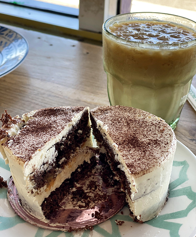 A slice of chocolate cake with cream frosting sits beside coffee like old friends catching up, both knowing they're better together.