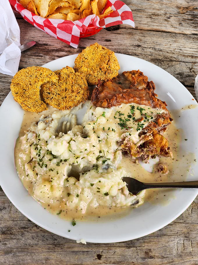 Chicken fried steak swimming in creamy gravy alongside golden-crusted fried green tomatoes. This plate is Texas comfort in its purest form.