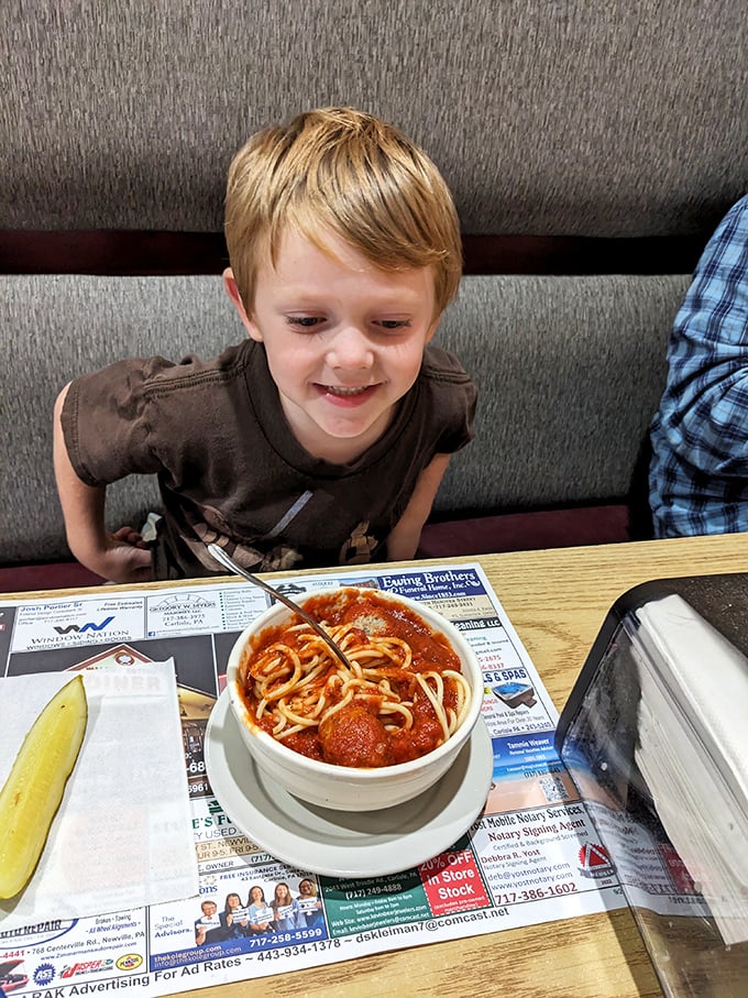 A young diner enjoying spaghetti and meatballs with the pure joy that only comes from twirling pasta at your favorite local spot. Future food critic in training.