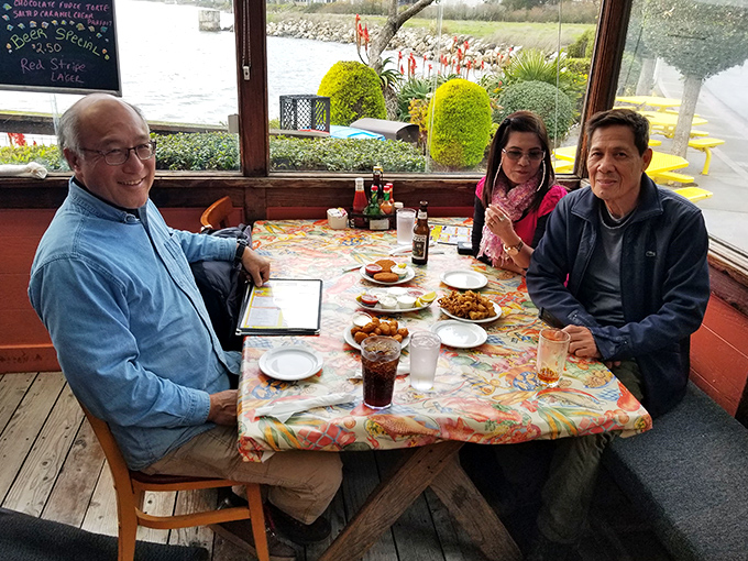 Happy diners by the window enjoying the harbor view with their feast. The colorful tablecloth somehow makes everything taste even better&mdash;it's seafood science.
