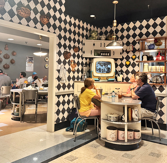 Families gather around kitchen tables while vintage TVs flicker with black-and-white memories. The checkered walls aren't the only things with patterns&mdash;so is the conversation.