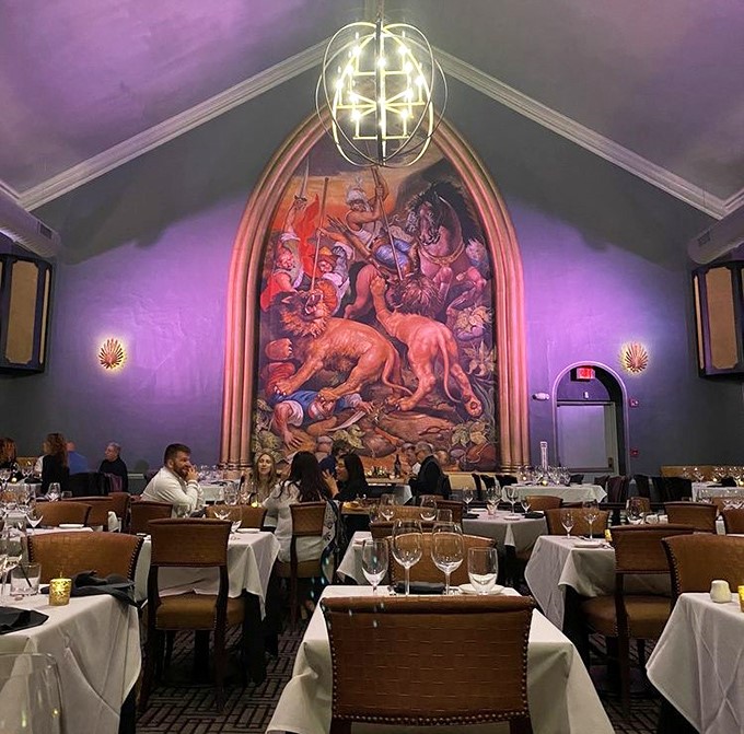 The dramatic lighting transforms dinner into theater, with that hunting mural serving as the backdrop for your own culinary performance.