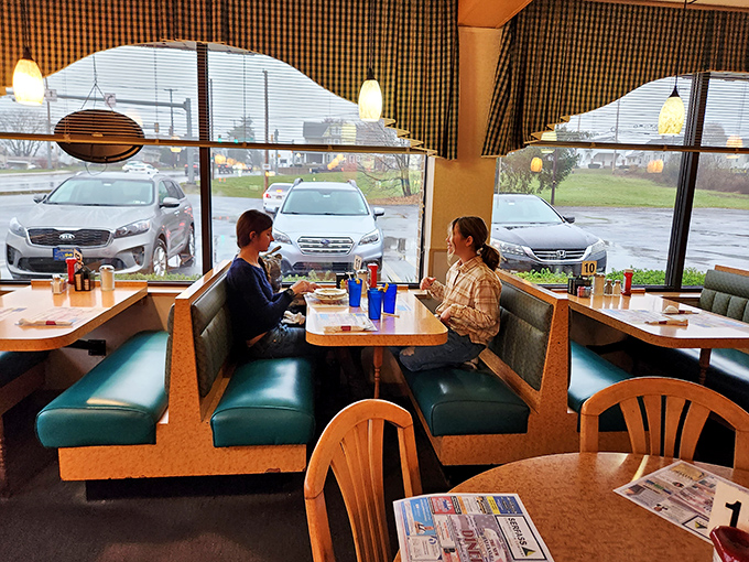 Rain-streaked windows frame the quintessential diner experience—conversations over blue glasses of ice water and menus that require two hands to hold.