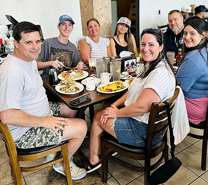 Happy diners gathering around breakfast&mdash;the universal language of morning joy spoken fluently at The Pancakery's wooden tables.