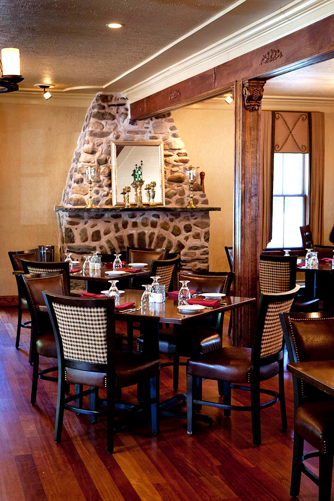 Stone fireplace and houndstooth chairs create an atmosphere where every meal feels like a celebration worth remembering.