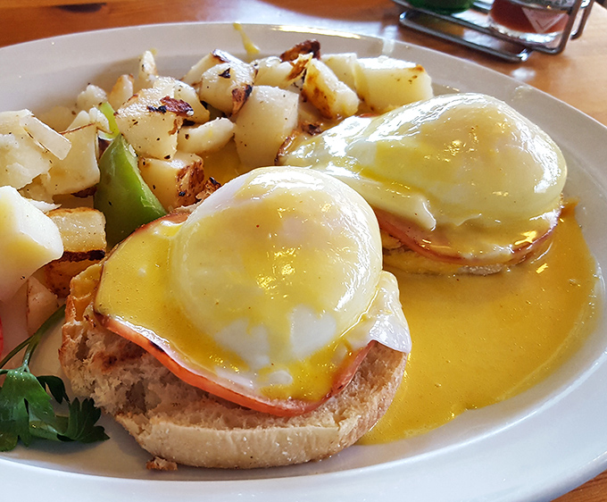 Eggs Benedict done right: perfectly poached eggs swimming in hollandaise sauce alongside crispy breakfast potatoes.
