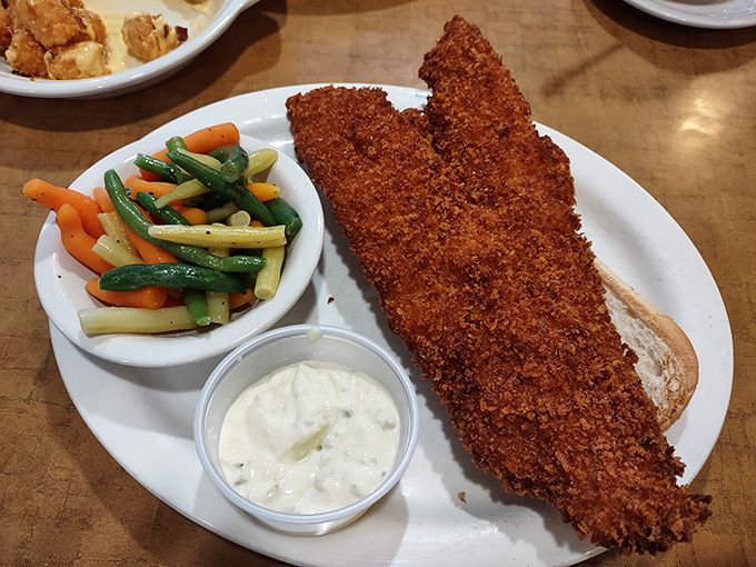 The fried cod sandwich arrives with a vegetable sidekick, proving that sometimes the best things in life are simple, crispy, and served with tartar sauce.