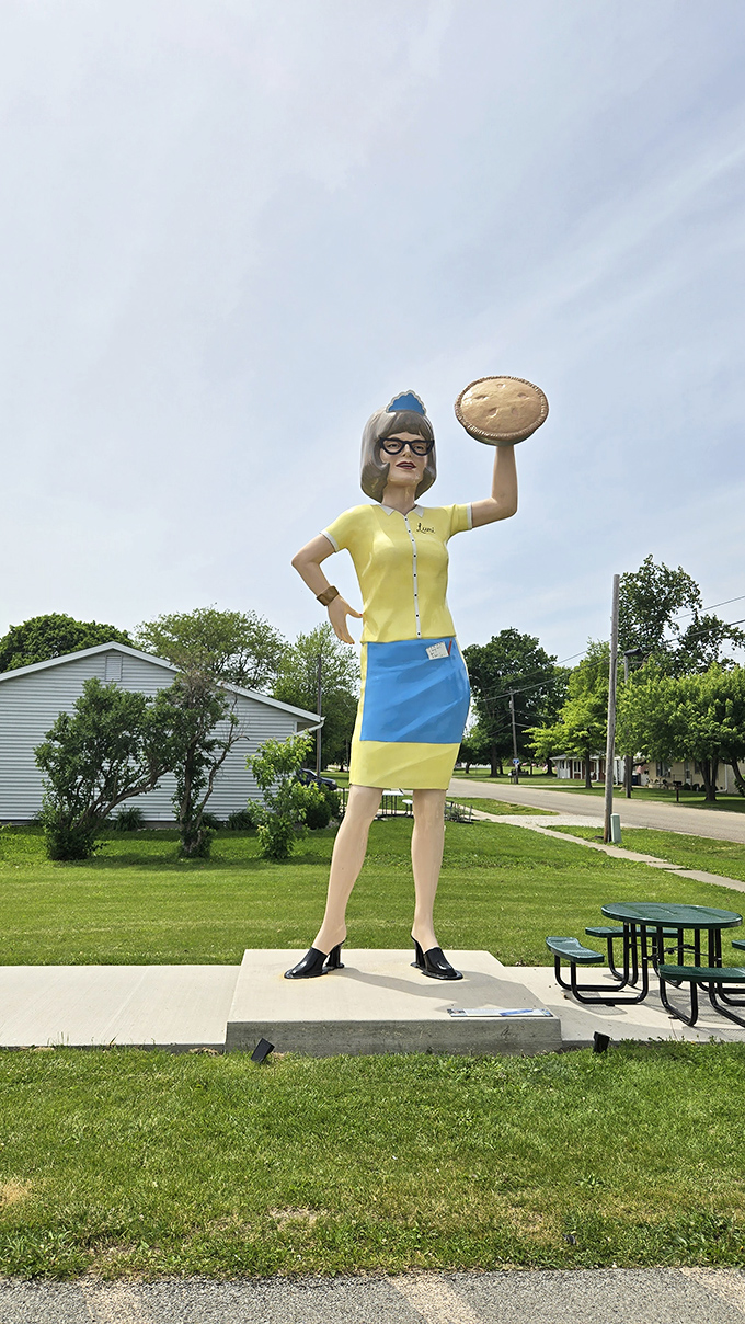 The Gemini Giantess holds her pie with mid-century confidence. In her yellow uniform, she's the retro waitress of your grandmother's road trip memories.