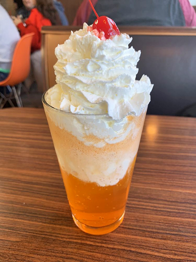 The orange float towers like a frothy skyscraper of nostalgia, topped with a cloud of whipped cream and that essential cherry beacon.