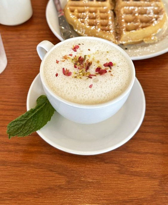 A pistachio rose latte that's dressed better than most people at brunch, topped with delicate petals and paired with golden waffles.