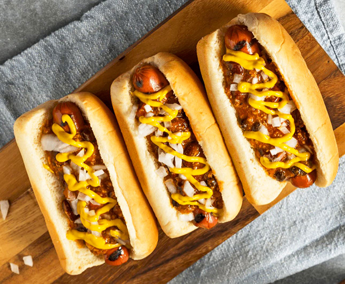 Three chili dogs lined up like soldiers ready for duty. The mustard zigzag isn't decoration&mdash;it's the yellow brick road to flavor town.