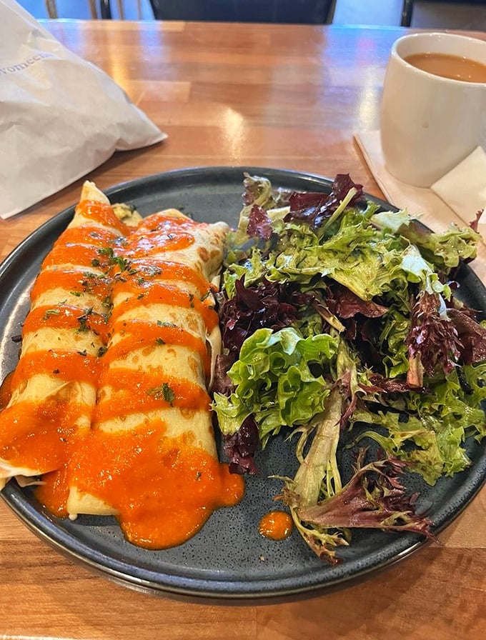 Savory crepes draped in vibrant sauce alongside fresh greens&mdash;proof that breakfast can be both sophisticated and deeply satisfying.