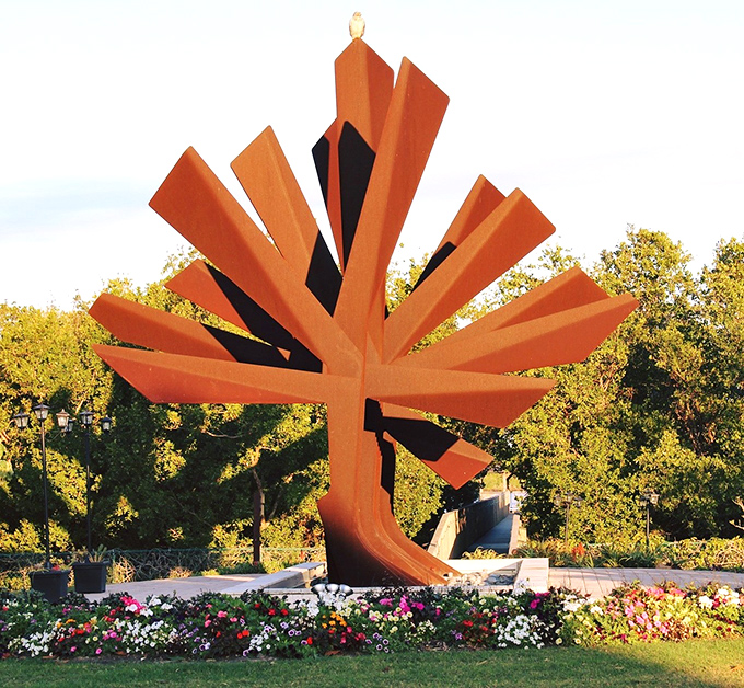This bold orange sculpture bursts from the earth like a geometric sunrise, proving that art can bloom just as brilliantly as flowers.