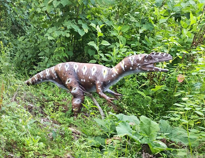 A smaller raptor model demonstrates the diversity of dinosaur species represented, its spotted coloration blending with the surrounding vegetation.
