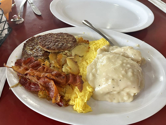 Breakfast perfection: crispy bacon, fluffy eggs, and savory sausage patties alongside potatoes smothered in country gravy that could make a vegetarian reconsider.
