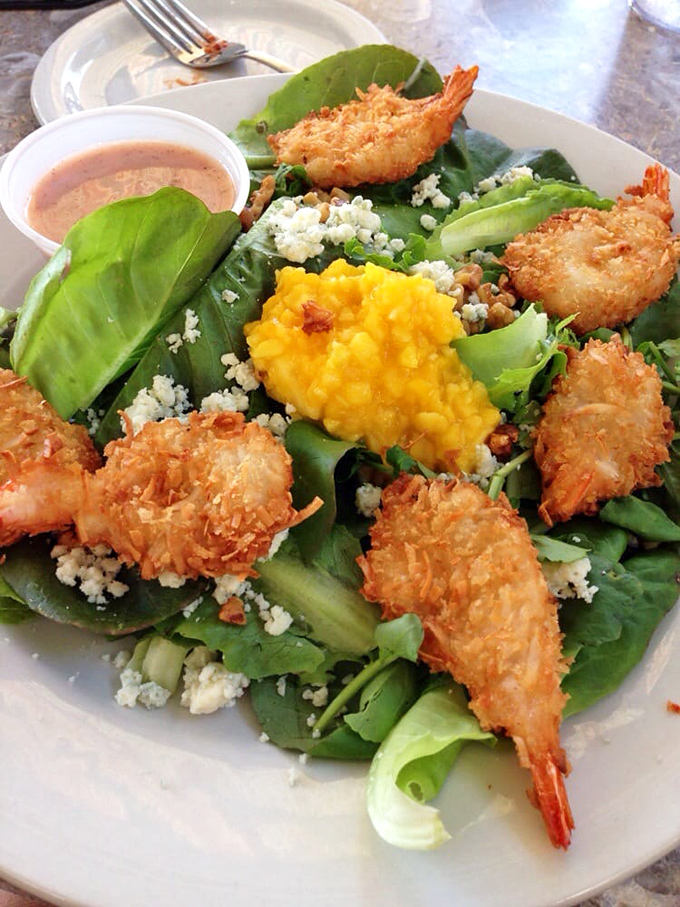 Coconut shrimp perched atop fresh greens like tropical sentinels guarding that vibrant mango treasure in the center.