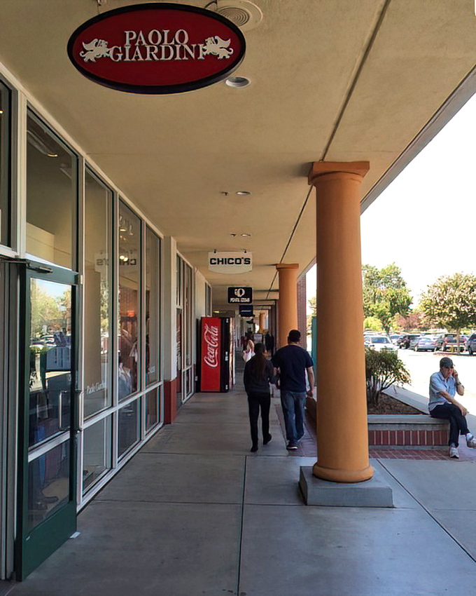 Paolo Giardini and Chico's storefronts create a retail canyon where shoppers drift between deals like explorers discovering new territories of markdown magic.