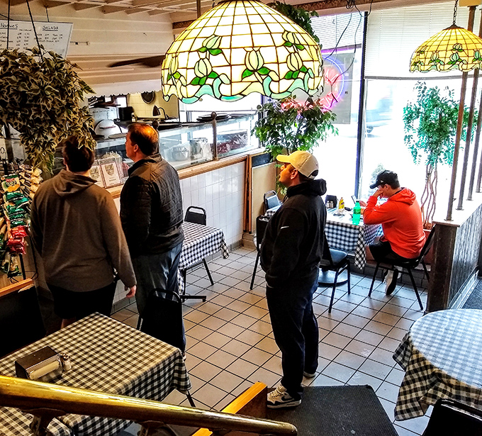 The line forms under vintage Tiffany-style lamps, where hungry patrons wait patiently for their turn at cheesesteak nirvana.