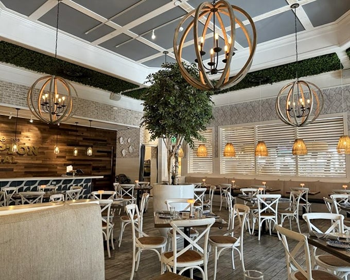 Wooden orb chandeliers hover above white cross-back chairs, creating a dining room that feels like Martha Stewart and a ship captain collaborated on the design.